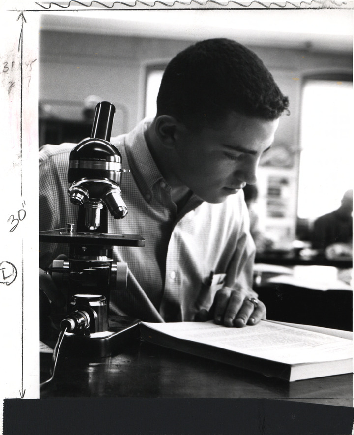 Student reading a book next to a microscope | Lehigh Preserve